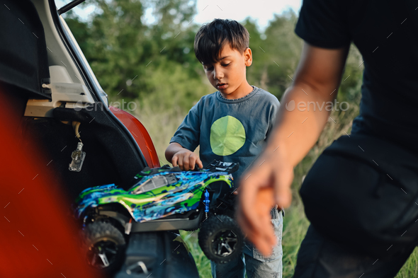 Boy is taking his toy race car out of open car trunk before driving it outside Stock Photo by ...
